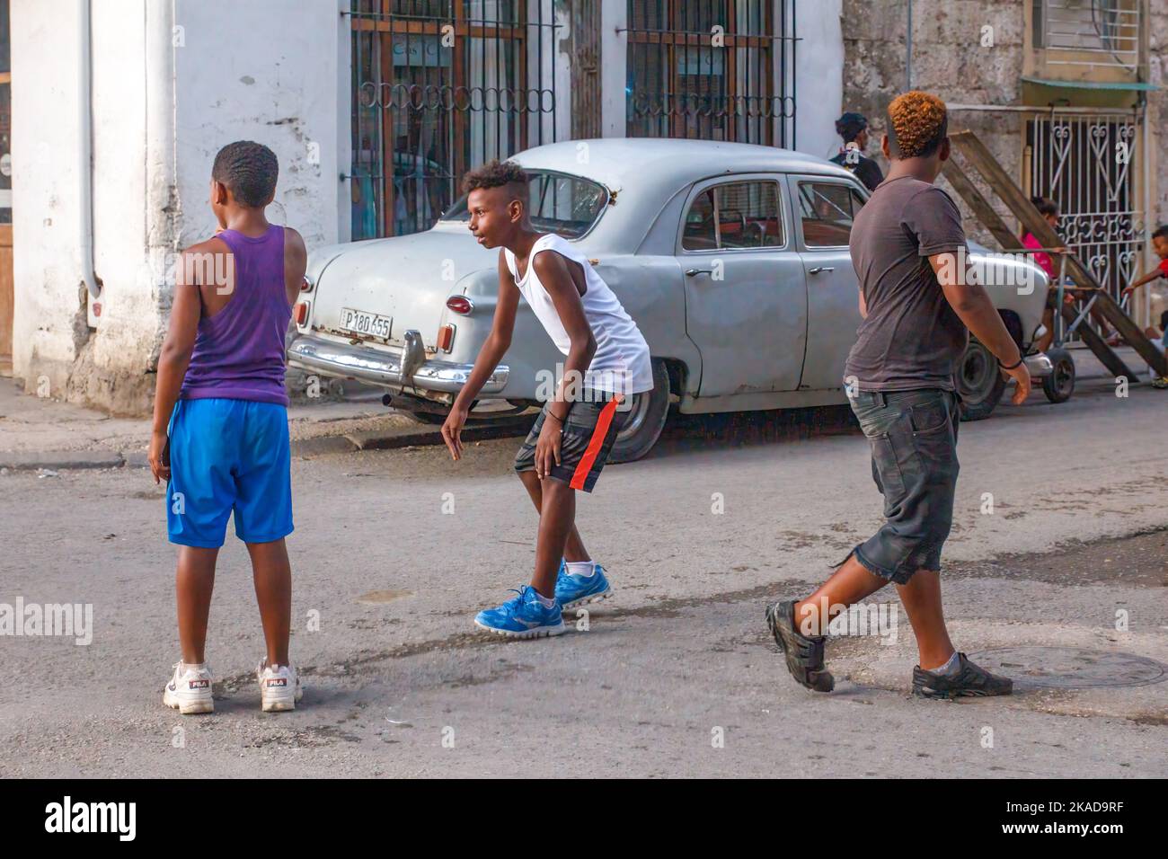 Two Cuban children are playing in the street by a gray vintage car. A ...