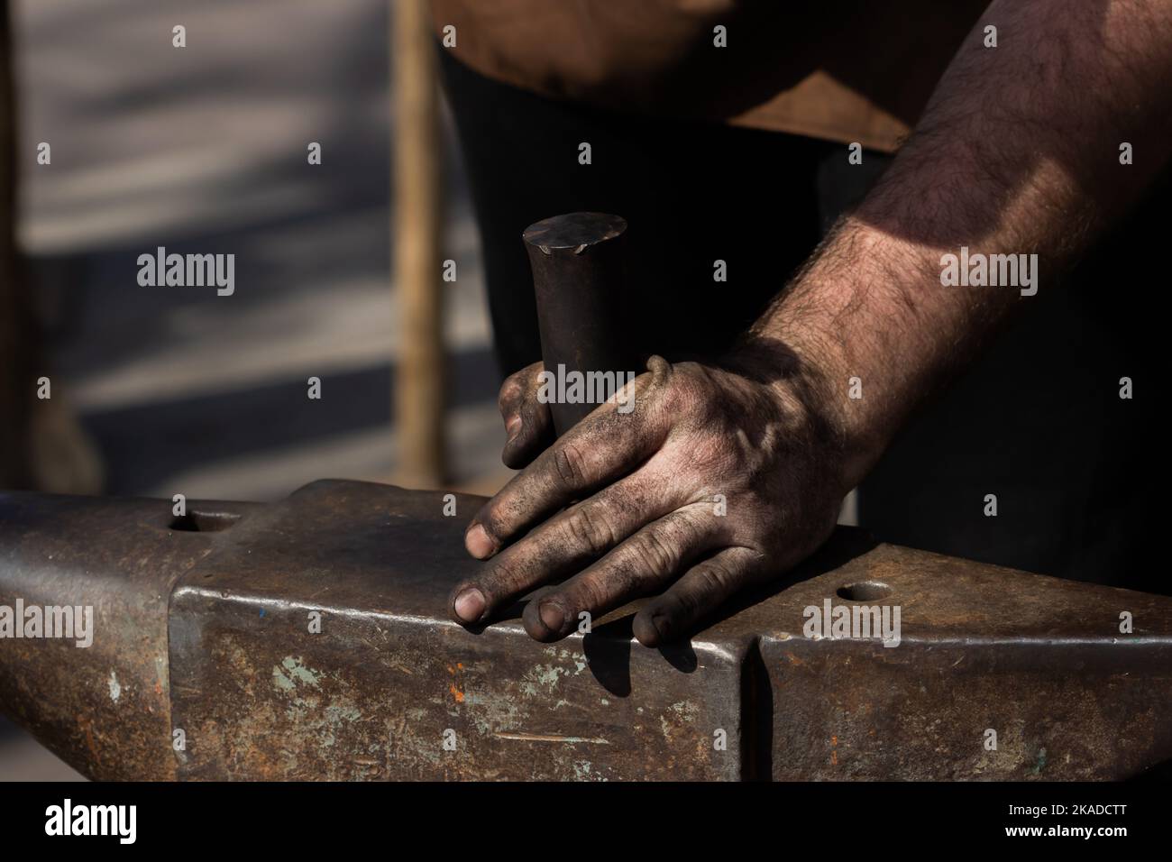 Unrecognizable blacksmith's hand holding a steel cylinder on an anvil ...