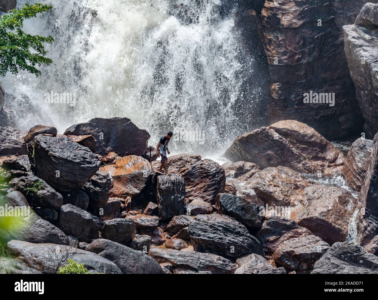 A young man walking on rock at a waterfall by the foot of Tepui ...