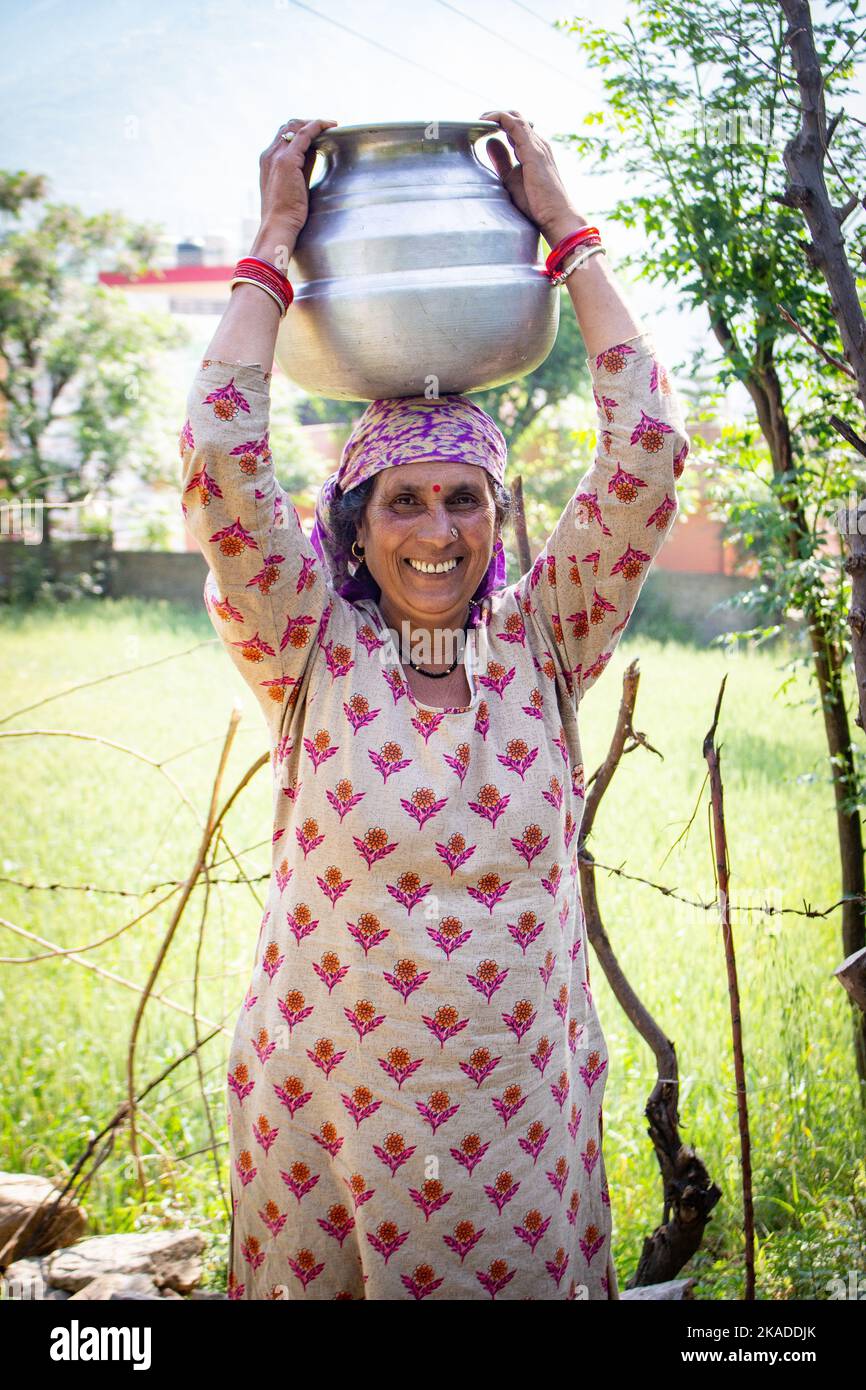 A vertical shot of an Indian woman carrying a metal water pitcher in a ...