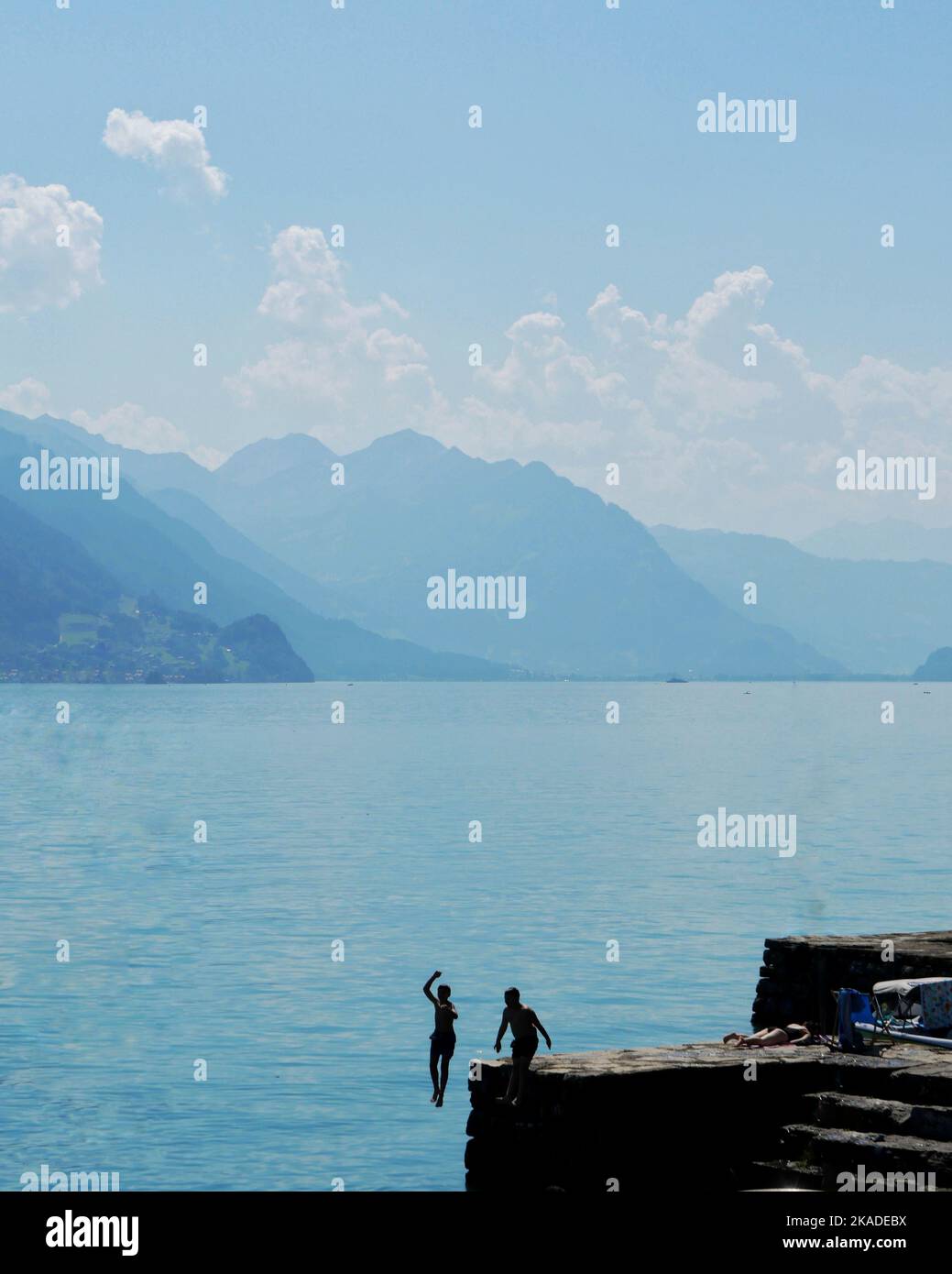 A vertical shot of a couple diving off a rocky cliff into the blue ...