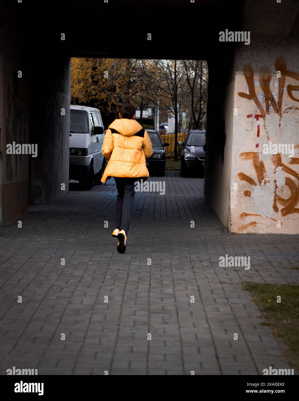 A vertical back view of a kid running on a cobblestone alley between ...