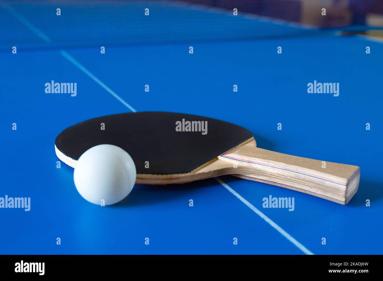 Wooden racket for ping pong and white ball lying on the blue table ...