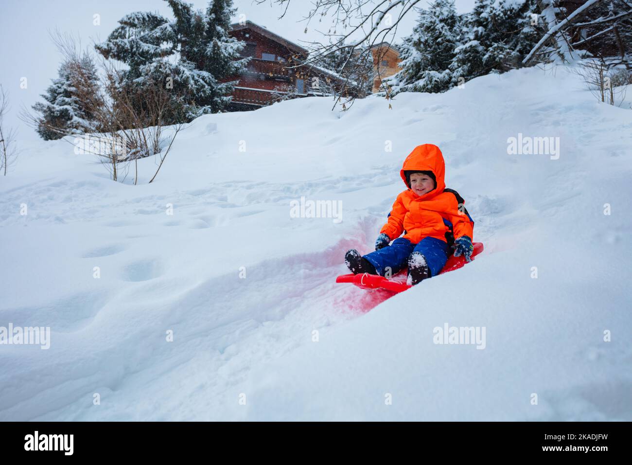 Happy boy in orange ski sport outfit go downhill on the sledge Stock ...