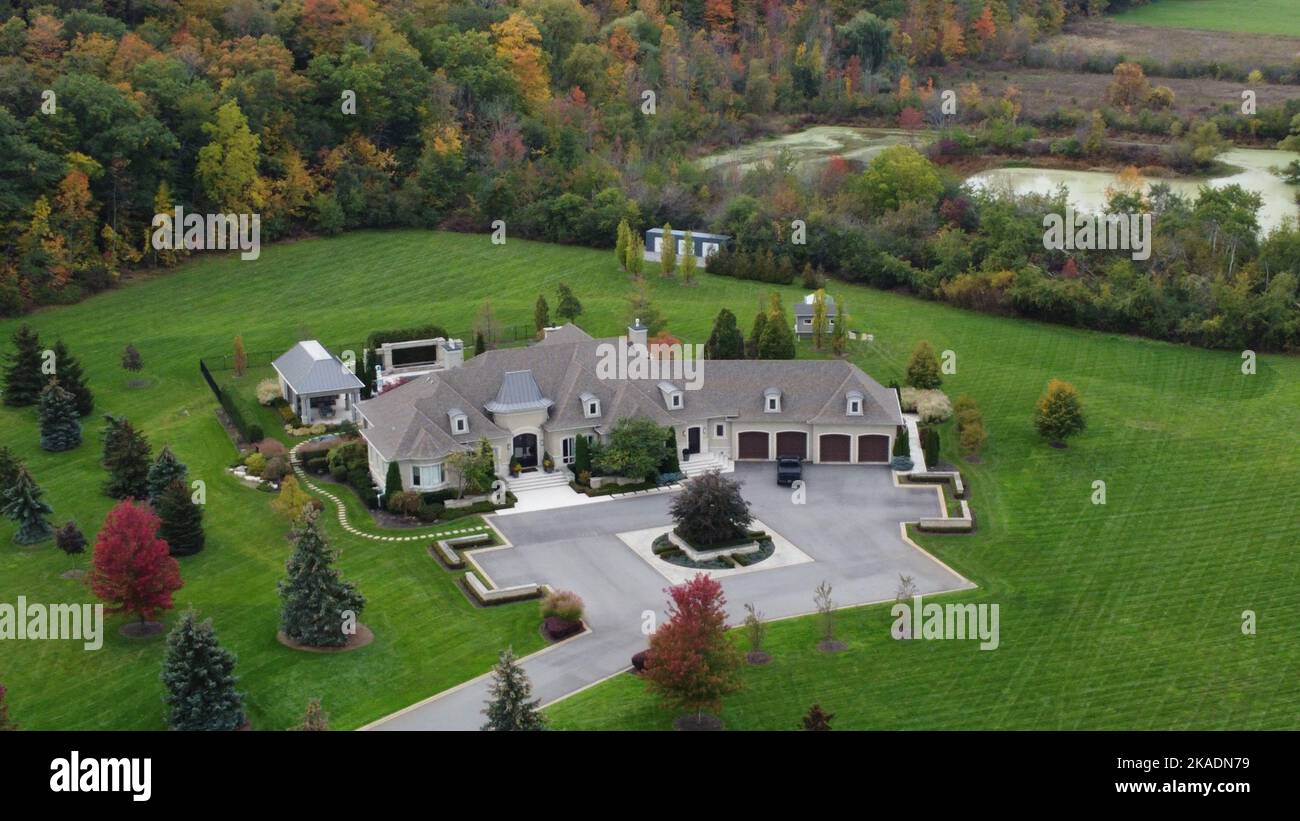 An aerial view of a beautiful mansion with a green lawn near a forest ...