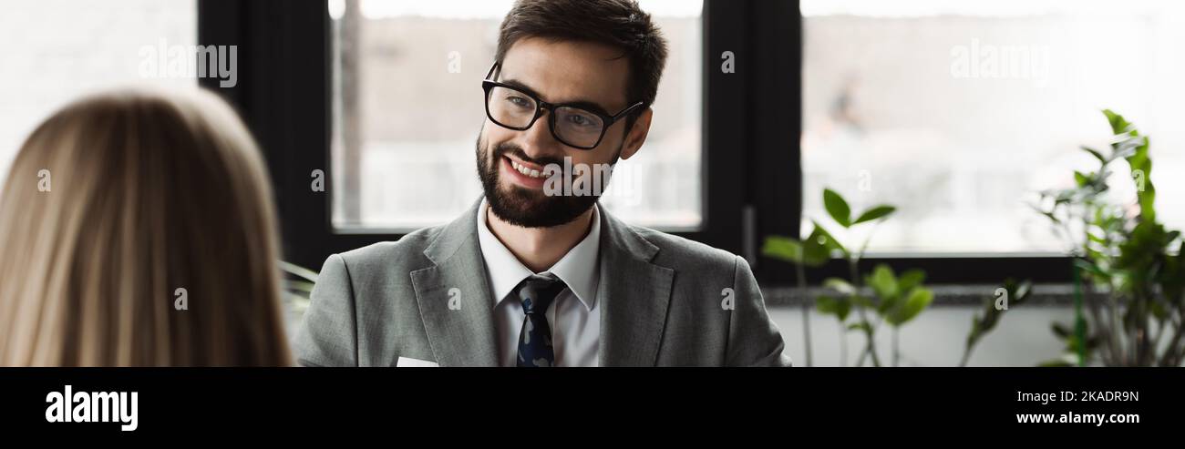 Cheerful businessman in suit looking at blurred woman on job interview ...
