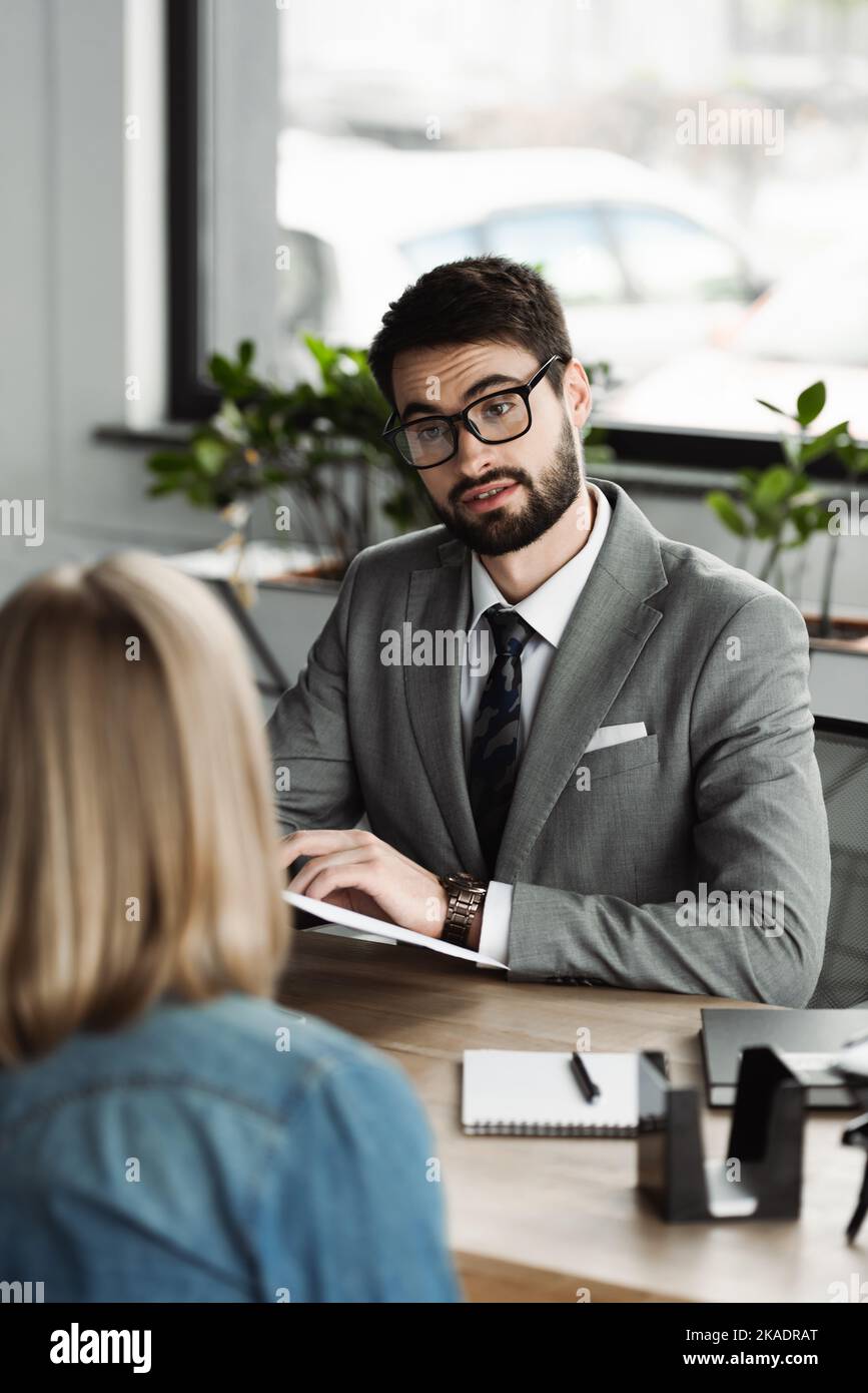 Businessman in formal wear holding resume and talking to blurred woman ...