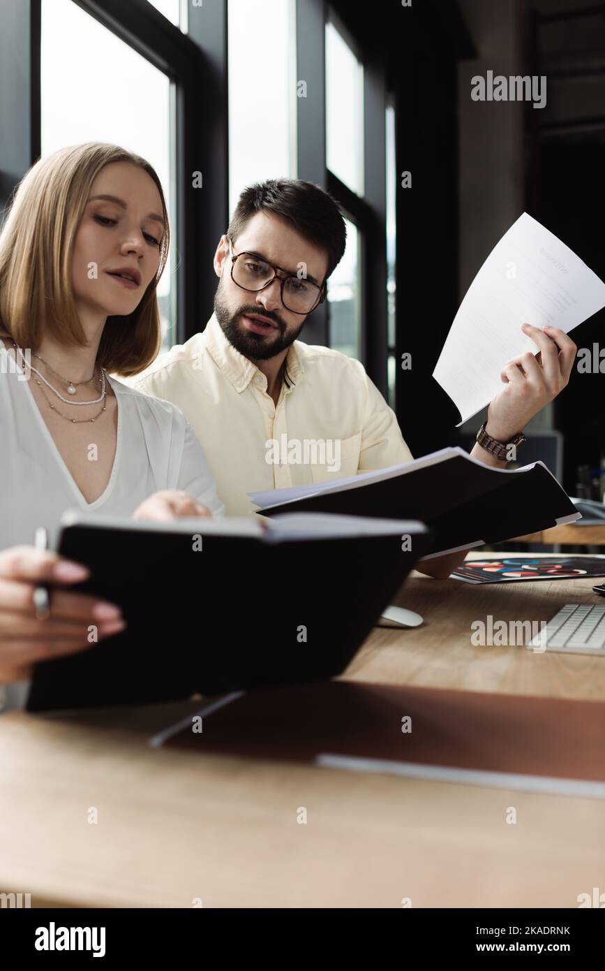 Businessman holding paper folder and talking to young intern with ...