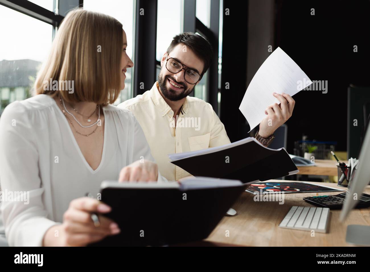 Positive manager holding paper folder and looking at new worker with ...