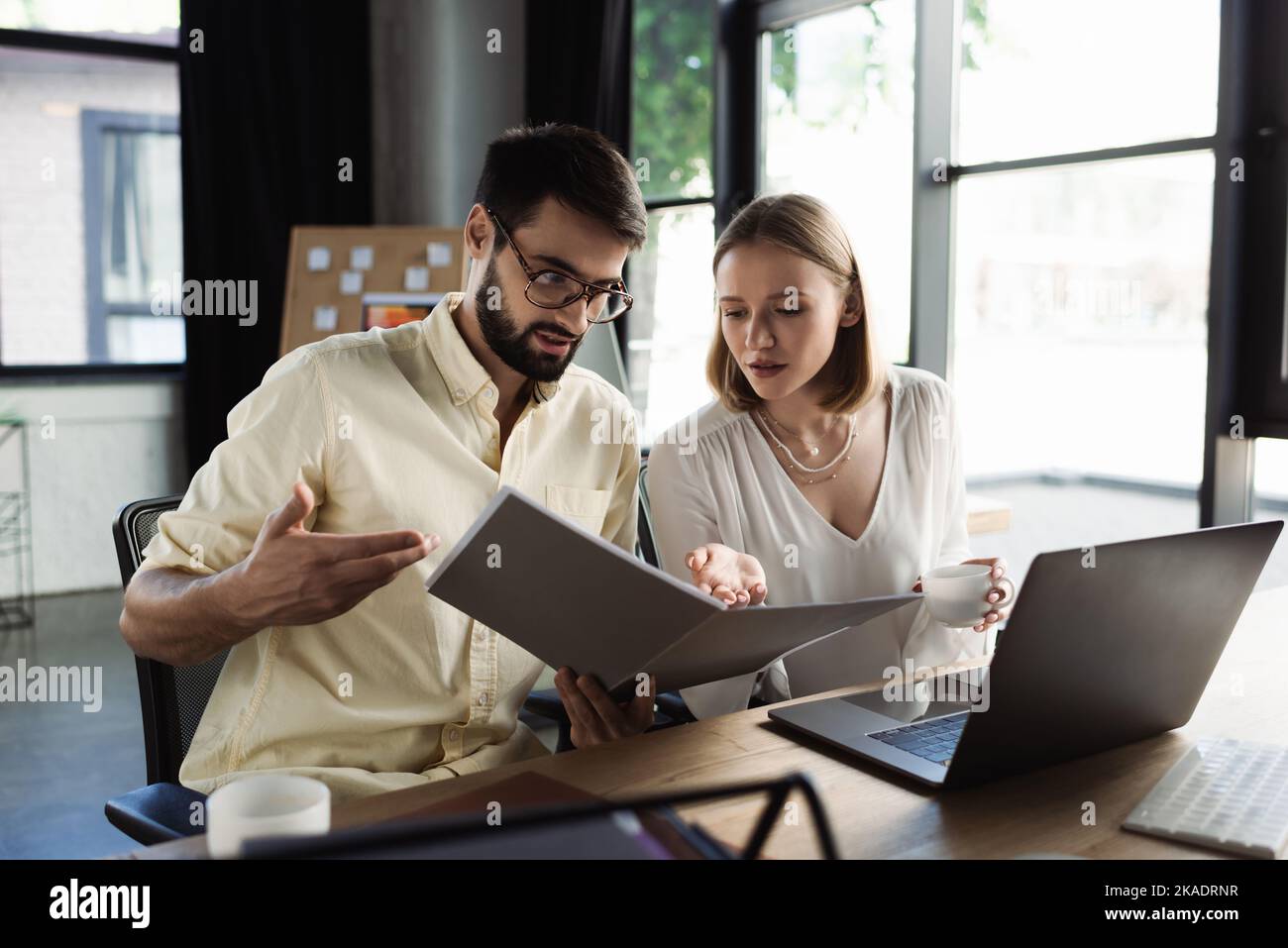 Businessman pointing at paper folder near intern with coffee and ...
