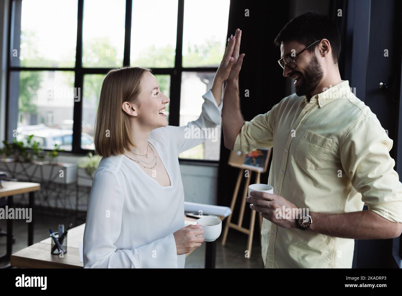 Side view of intern and manager with coffee cups giving high five in ...