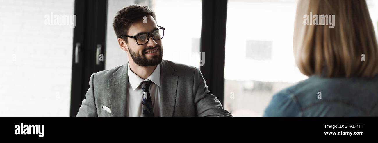 Positive businessman in formal wear looking at blurred woman during job ...