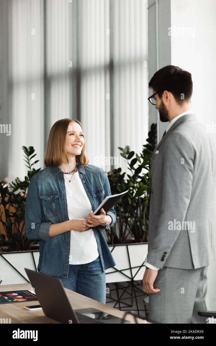 Smiling job seeker holding paper folder near businessman during ...