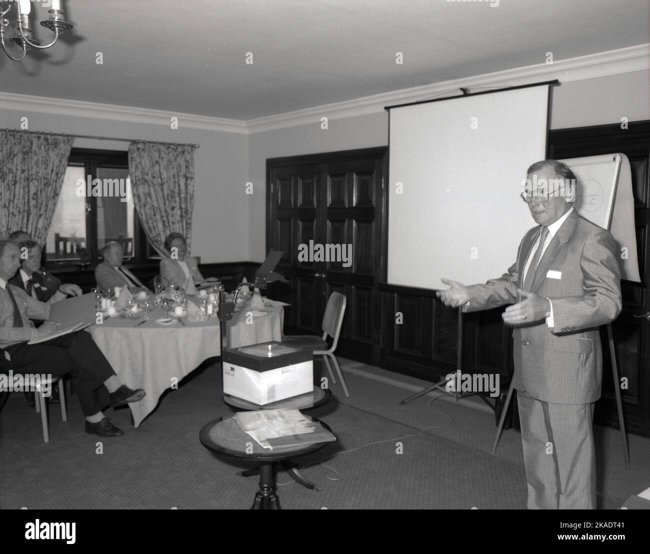 1980s, historical, in a hotel conference room, a suited male presenter ...