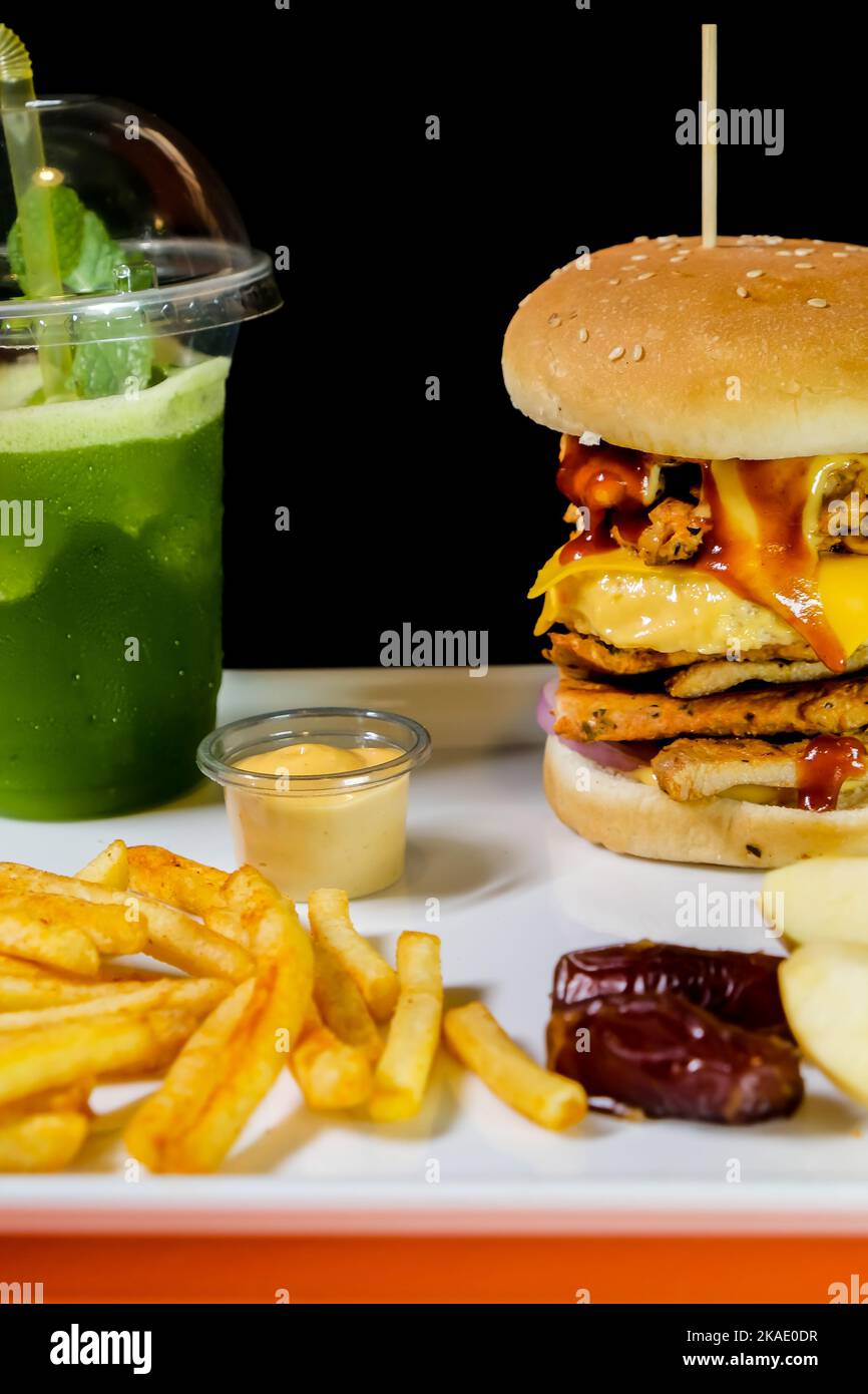 A closeup shot of a burger, french fries and dipping sauce with pieces ...