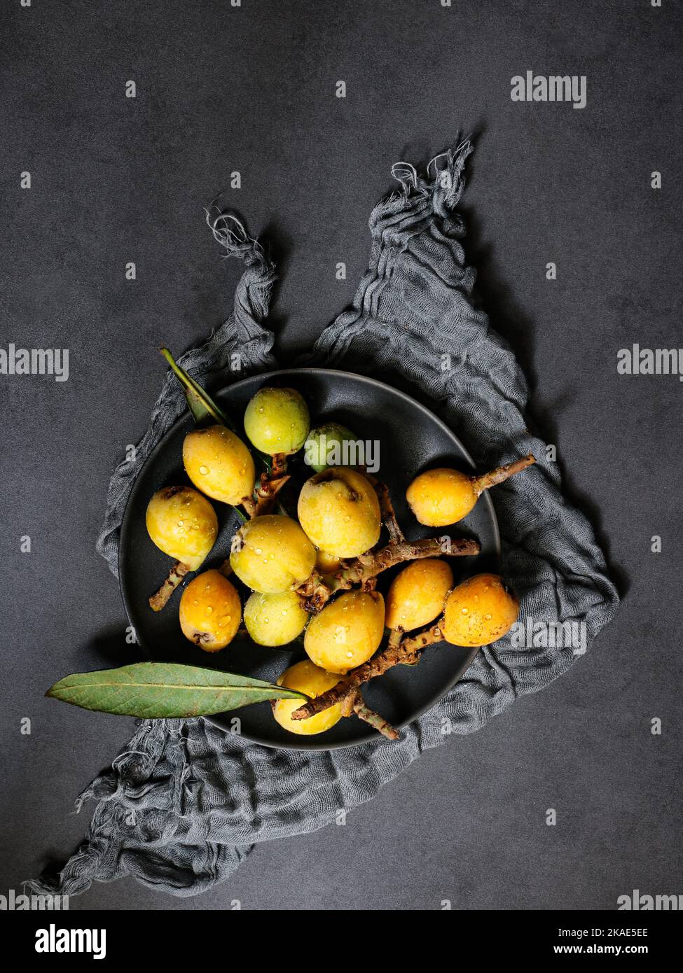 A top view shot of a plate of loquats on a grey fabric Stock Photo - Alamy
