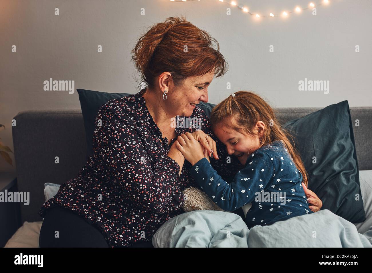 Mother playing with her little daughter in bed, having fun before going sleep. Mom tickling her ...