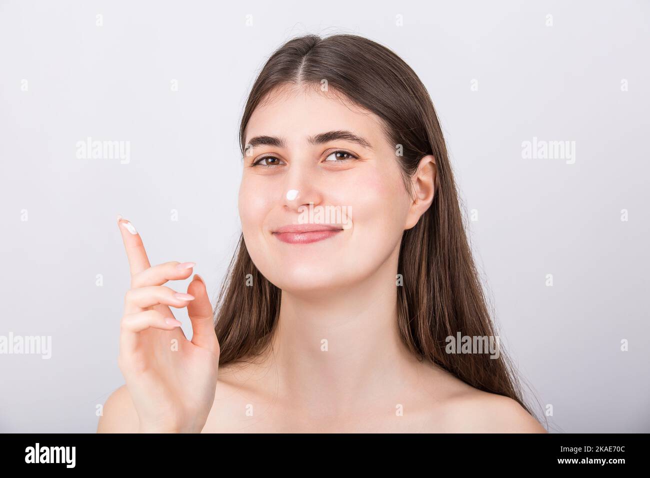 Funny young woman apply moisturizing cream on the top of her nose ...
