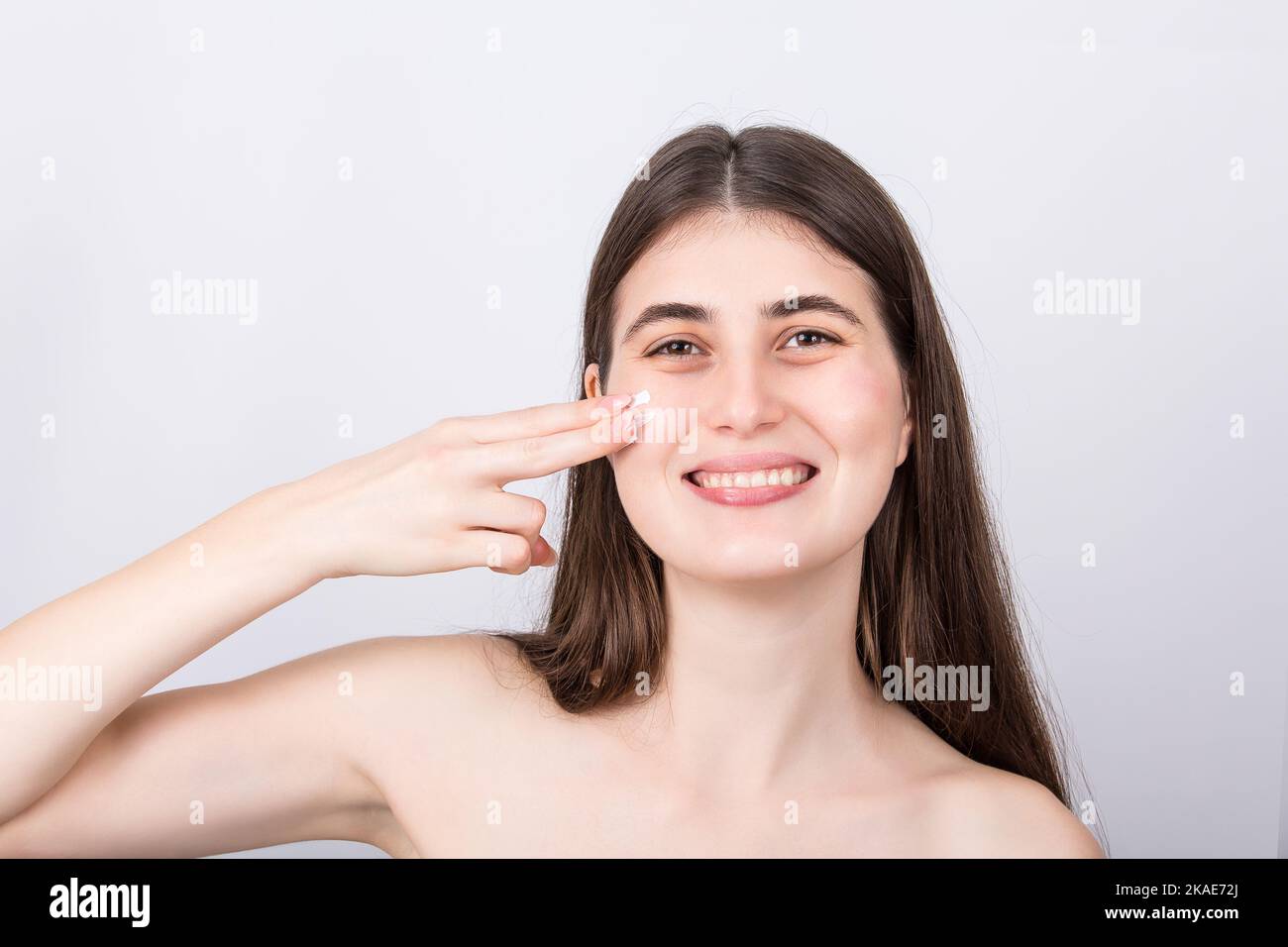Excited young woman spreads moisturizing cream on her cheek, looking ...