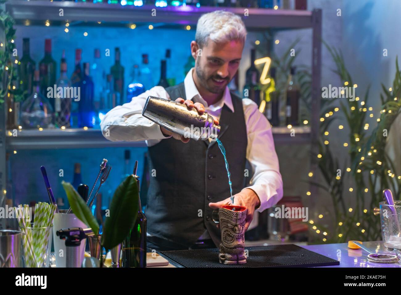 Professional barman in a white shirt and black apron making blue ...