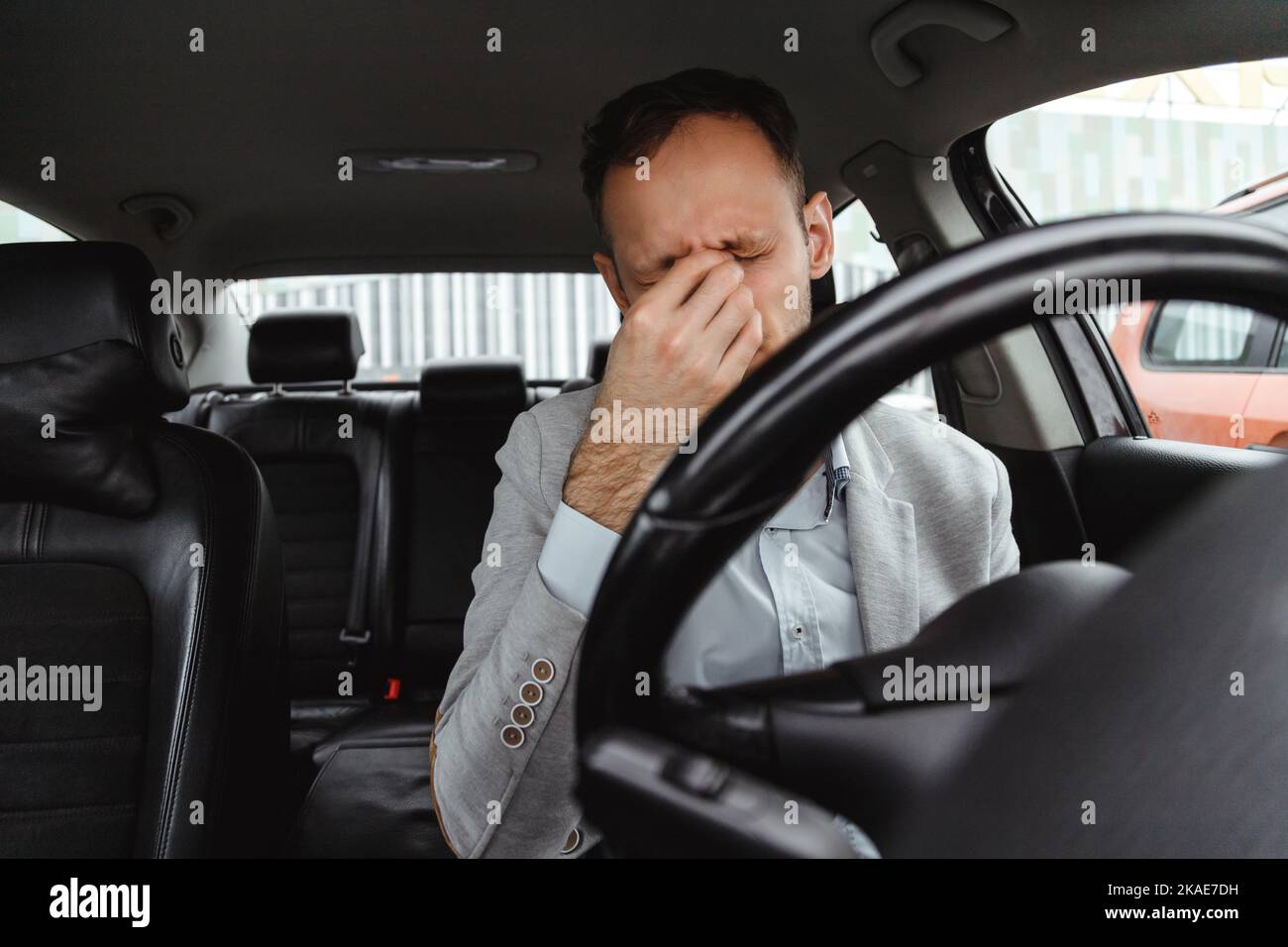 Tired man driver in suit rubbing his eyes behind steering wheel of car ...