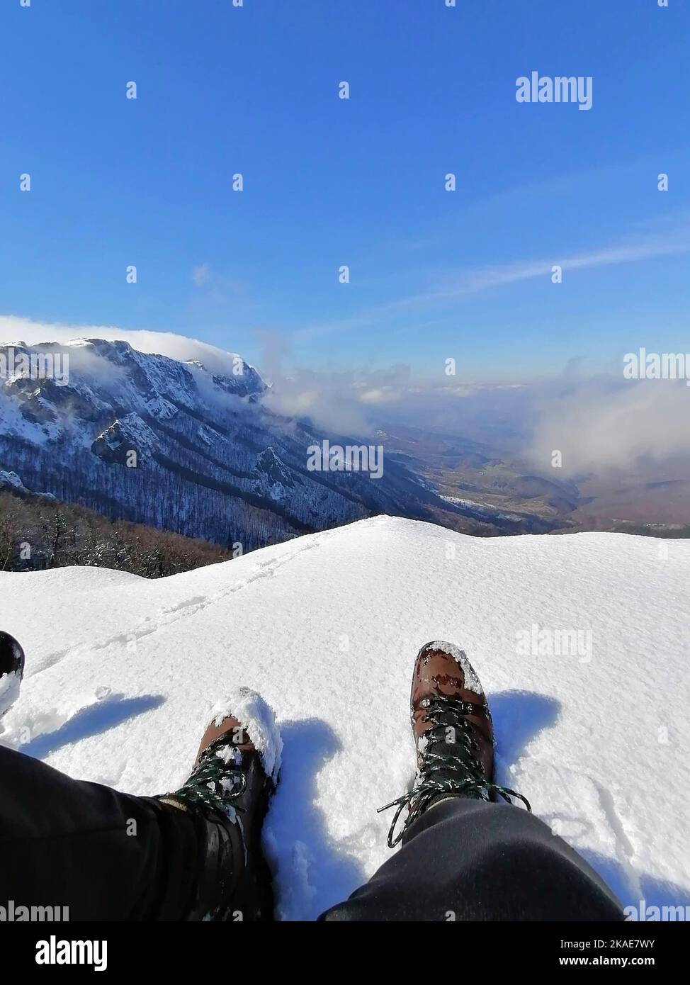 A vertical shot of man's feet sitting on the edge of a hill with snow ...