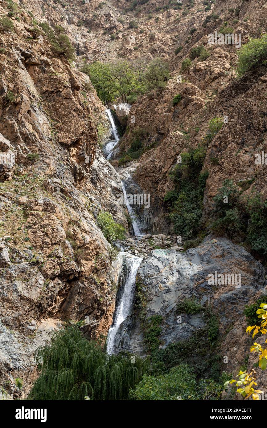A vertical shot of a small waterfall surrounded by big rocks and cliffs ...