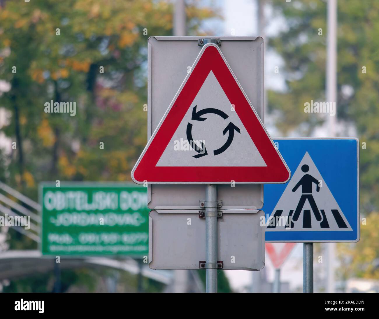 A red and white roundabout sign with a pedestrian crossing sign in the ...