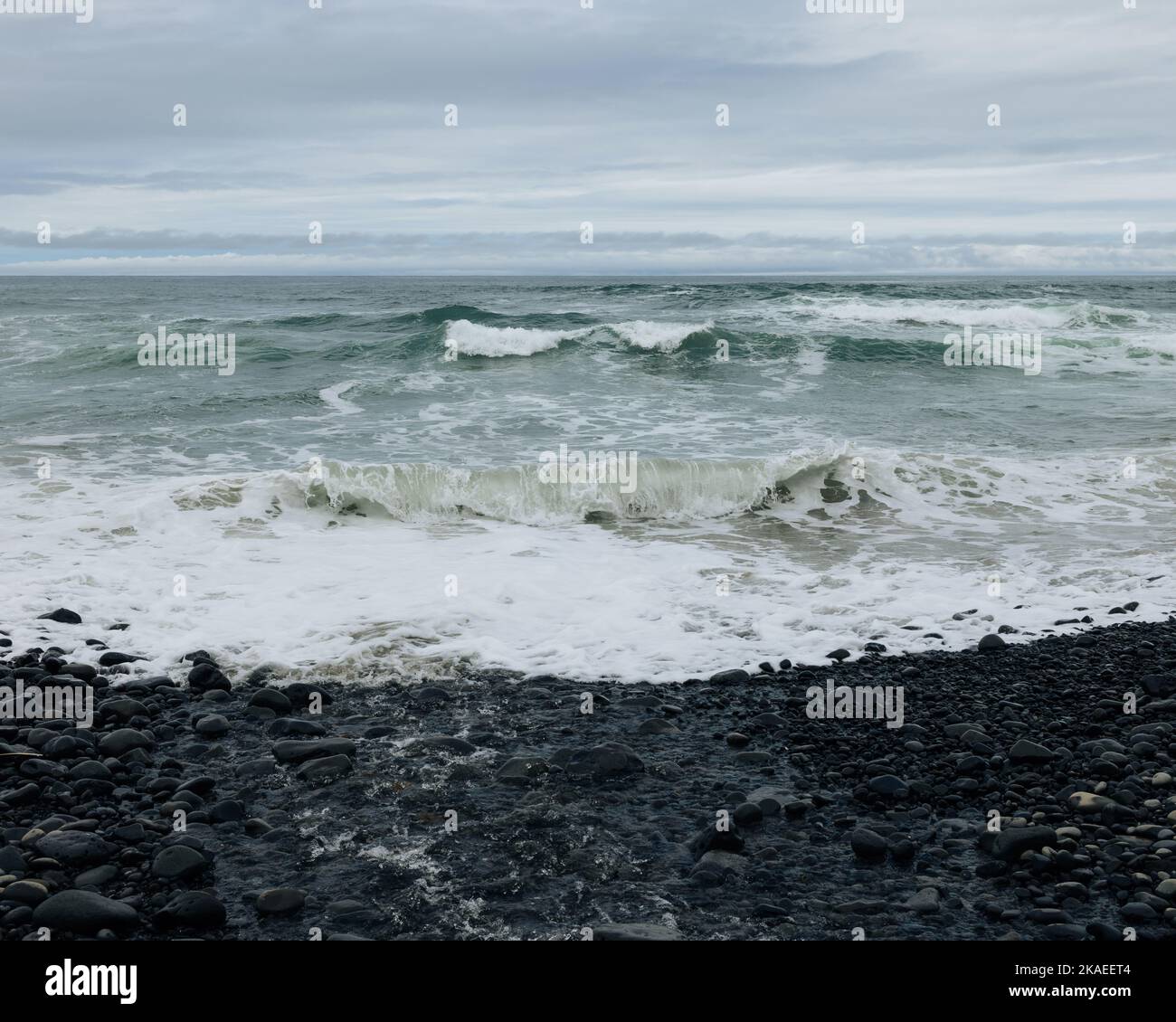 A scenic view of ocean waves washing the pebbles beach on a cloudy day ...