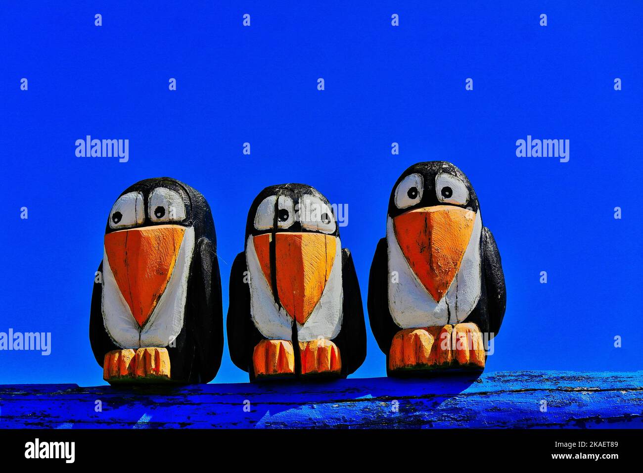 A blue log with three sculptures of penguins made of wood on a blue ...
