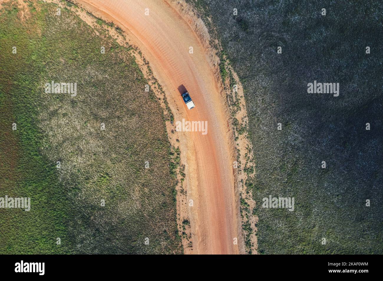 A top view of the sandy road with a passing car surrounded by a green ...