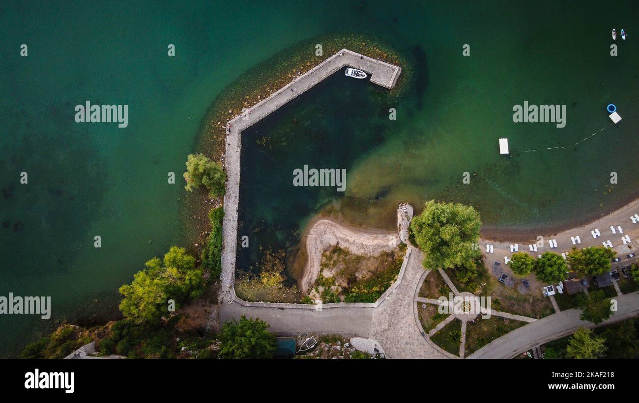 An aerial view of small boat by the concrete dock in shallow green sea ...
