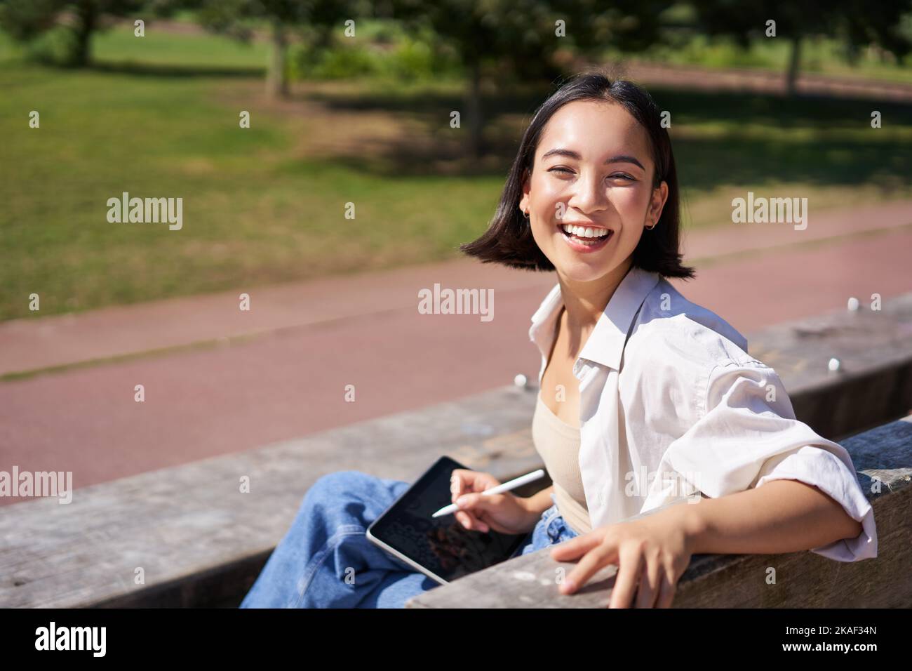 Happy korean woman sitting on bench with digital tablet and graphic pen ...