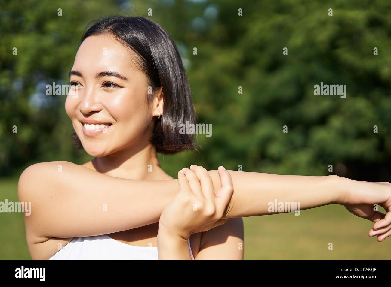 Portrait of young fitness woman stretching her arms, warm-up before training session, sport ...