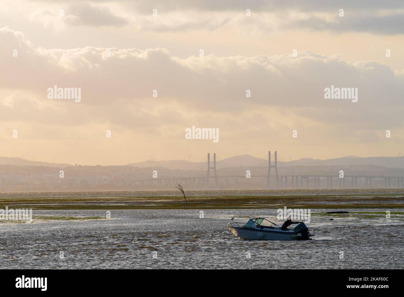 A side view of a fisherman steering a small motor boat, and the sunset ...