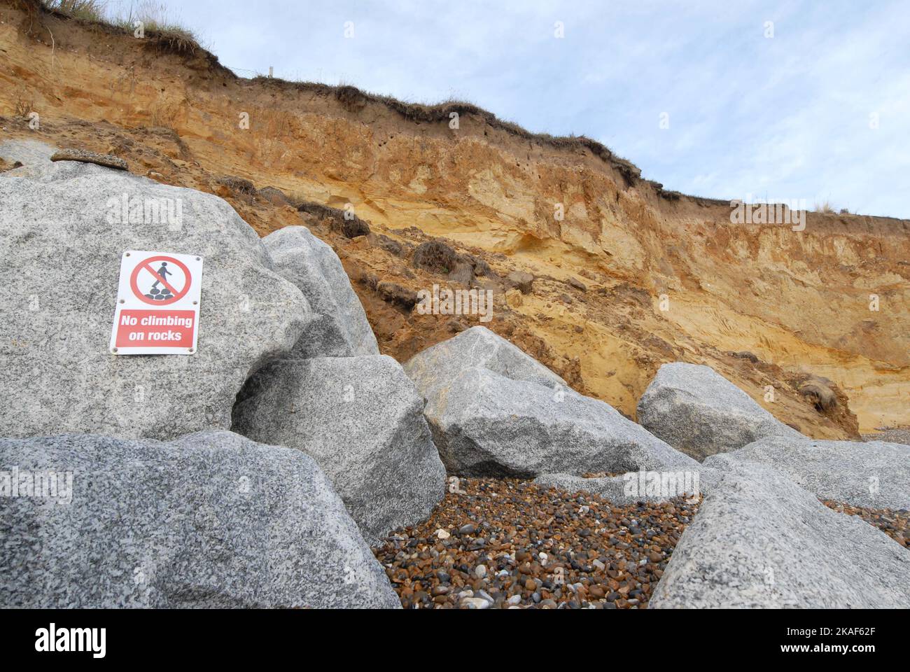 Sign saying no climbing on rocks, on flood defence in front of cliffs ...