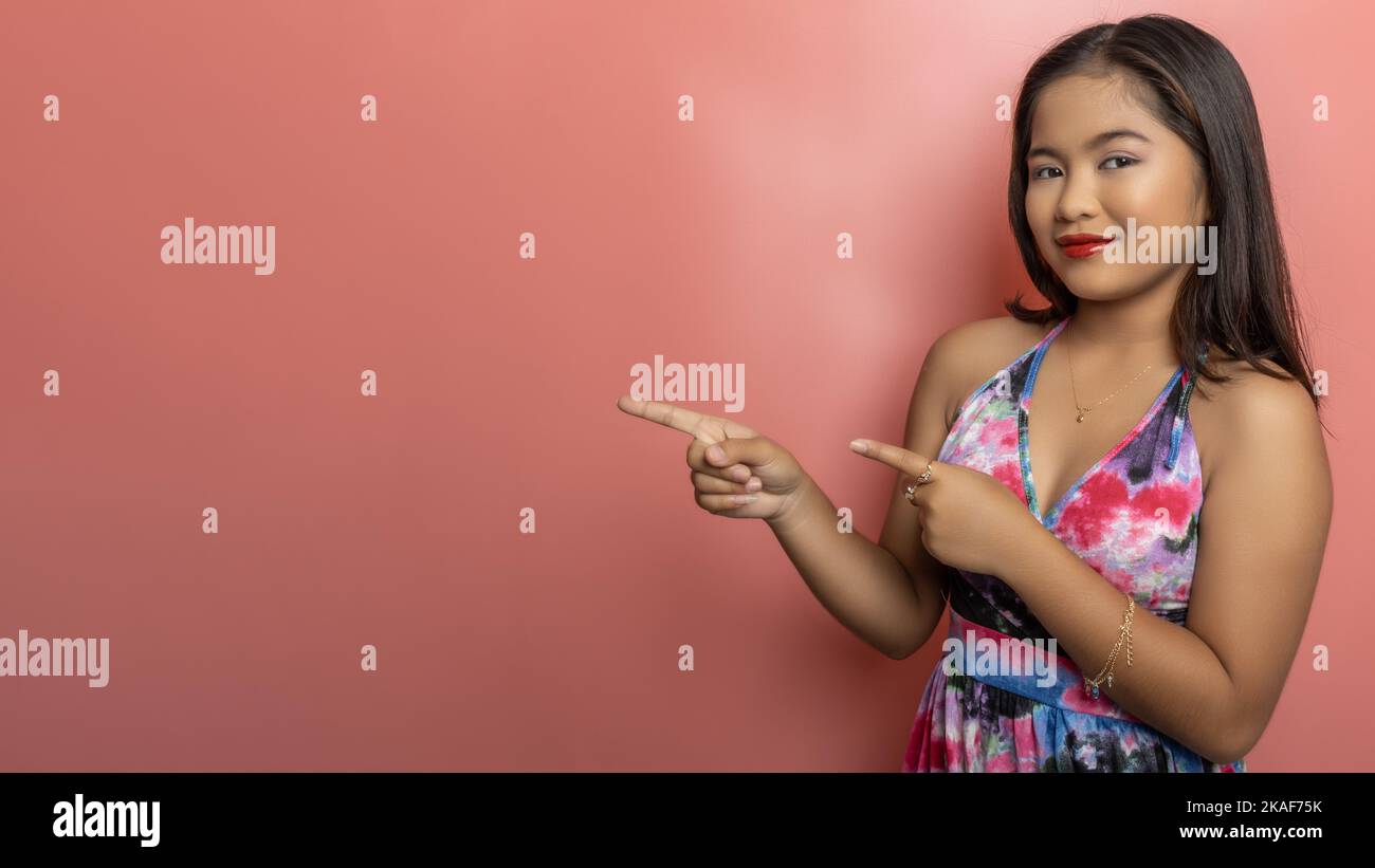 A Filipina in a colorful dress smiling and pointing to the side with ...