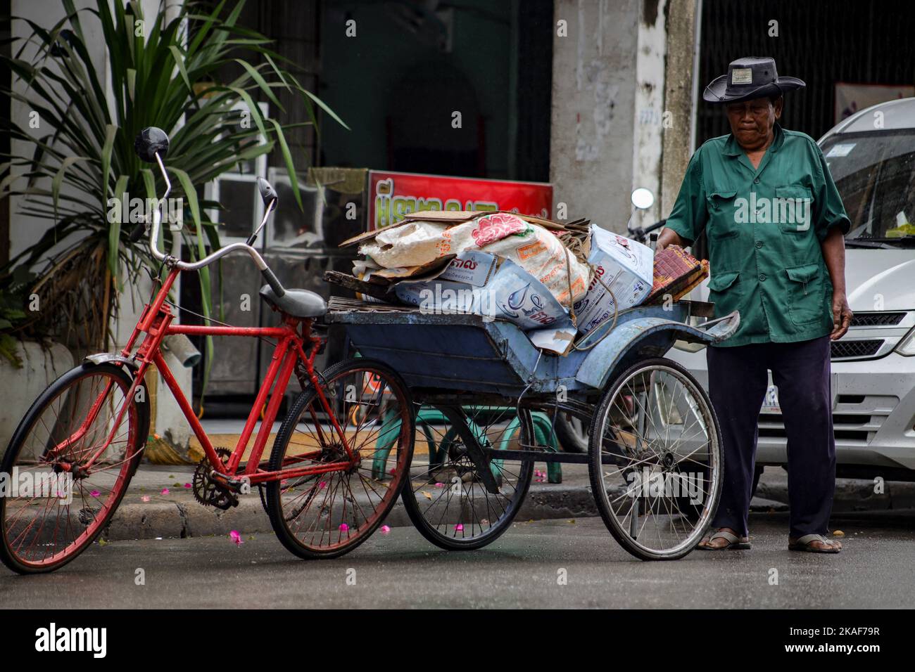 A poor Cambodian person walking with his personal belongings on a bike ...