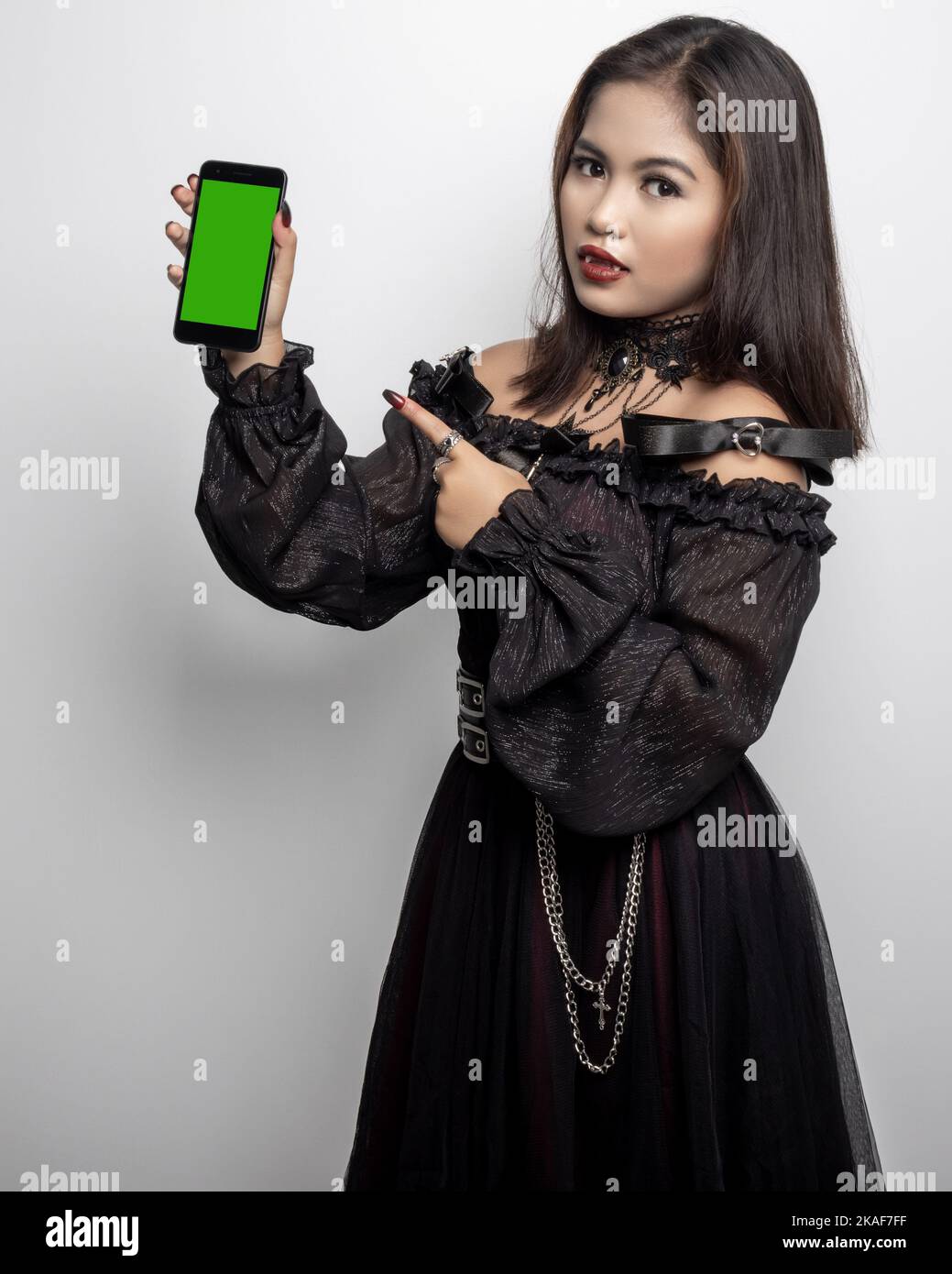A Filipina in a vampire costume pointing at a phone with a green screen ...