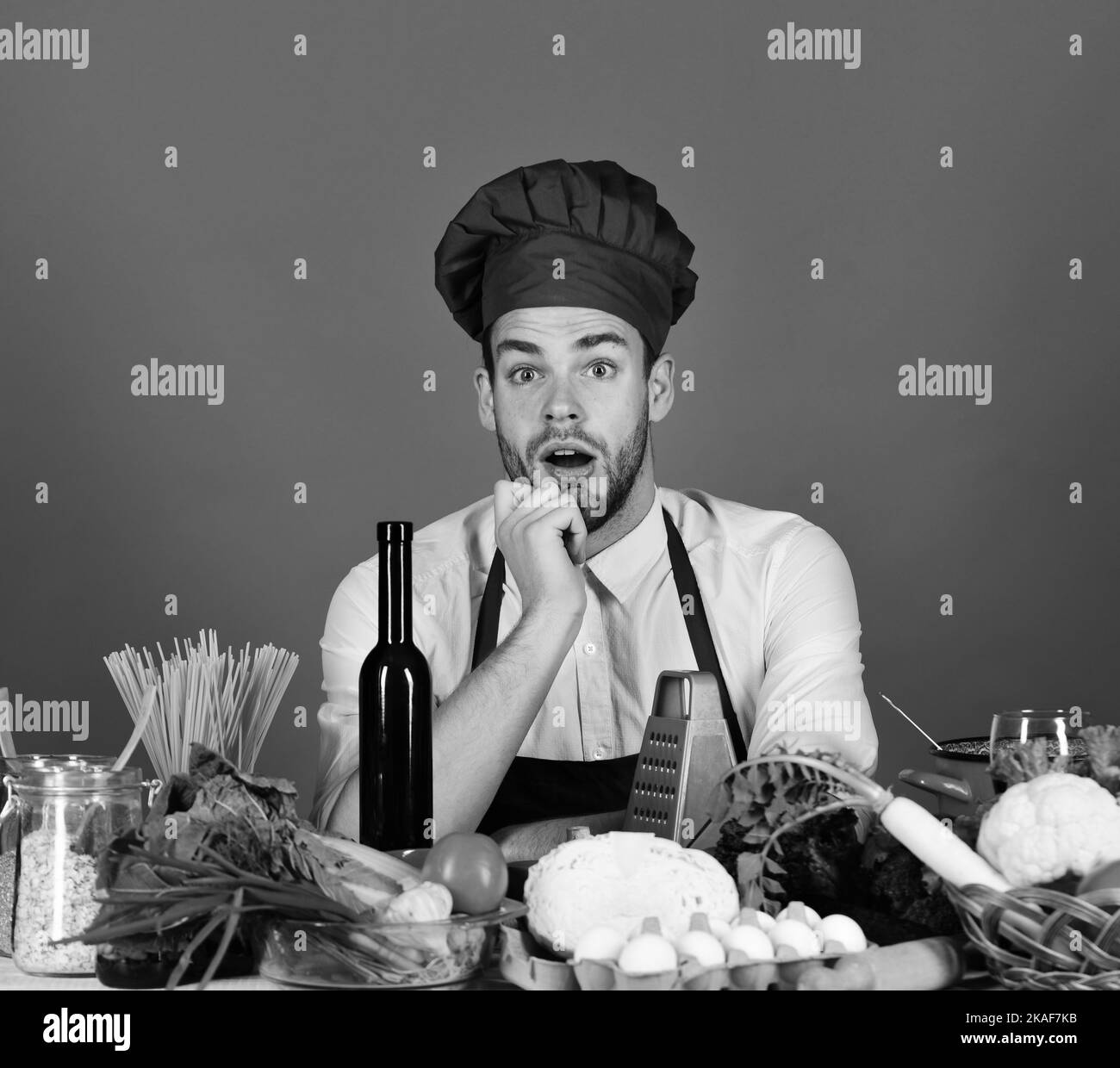 Chef with surprised face sits by food on red background Stock Photo - Alamy
