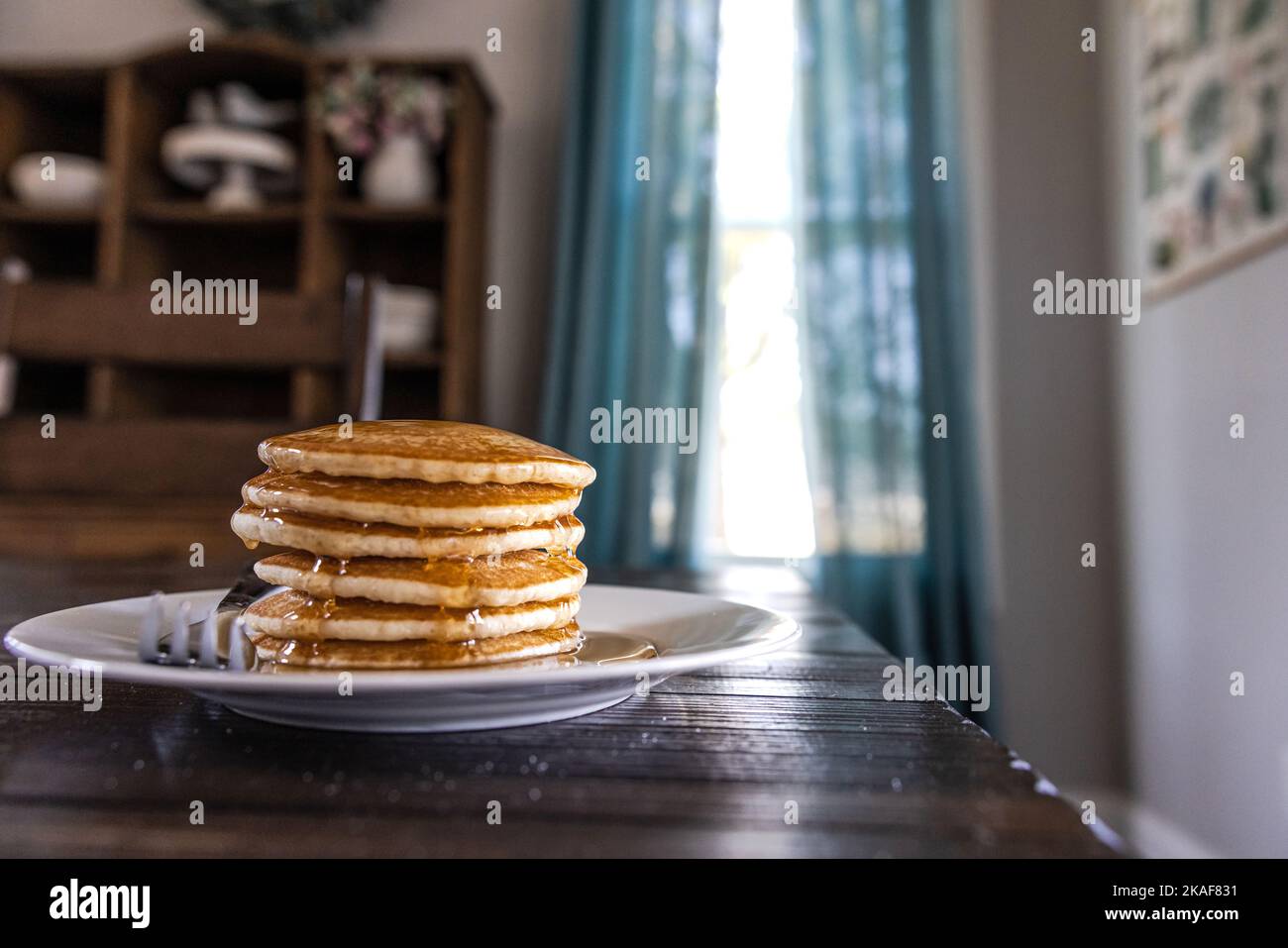 A plate with a stack of homemade pancakes at a dark wood kitchen dining ...