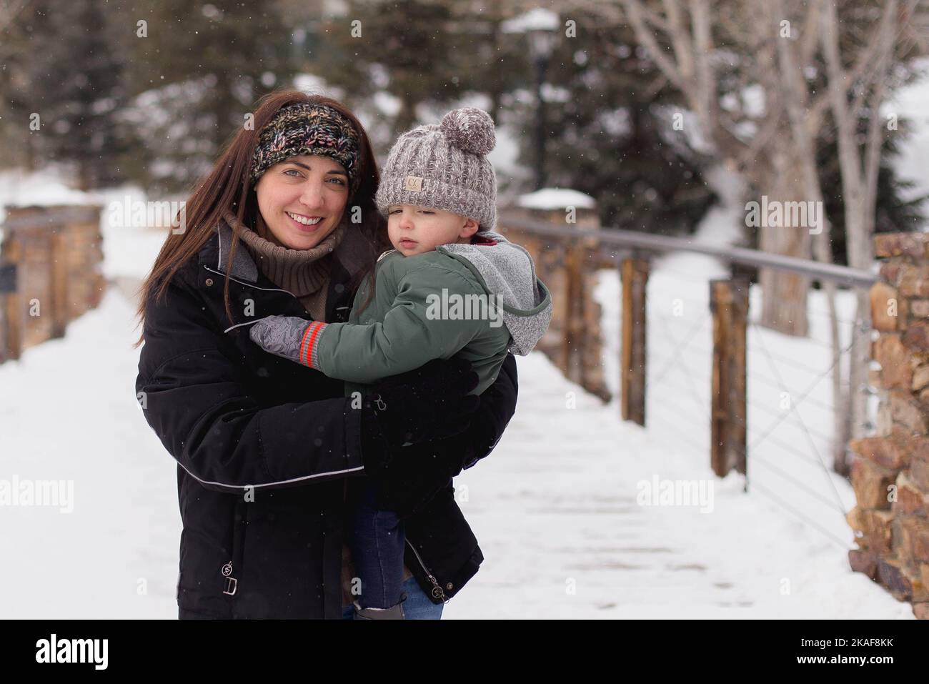 A smiling white woman hugging her baby boy wearing a C.C beanie on a ...