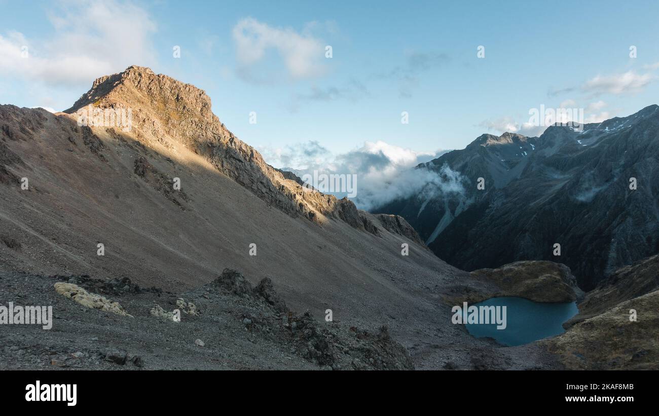 A scenic view of rocky mountains with a small pond under the blue sky ...