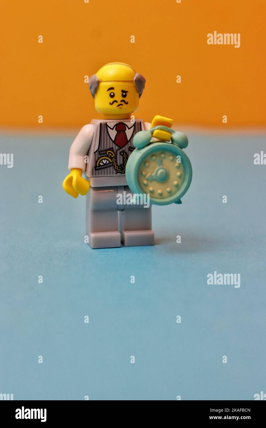 A toy male figure with a vest and tie holding a clock with a frown on ...