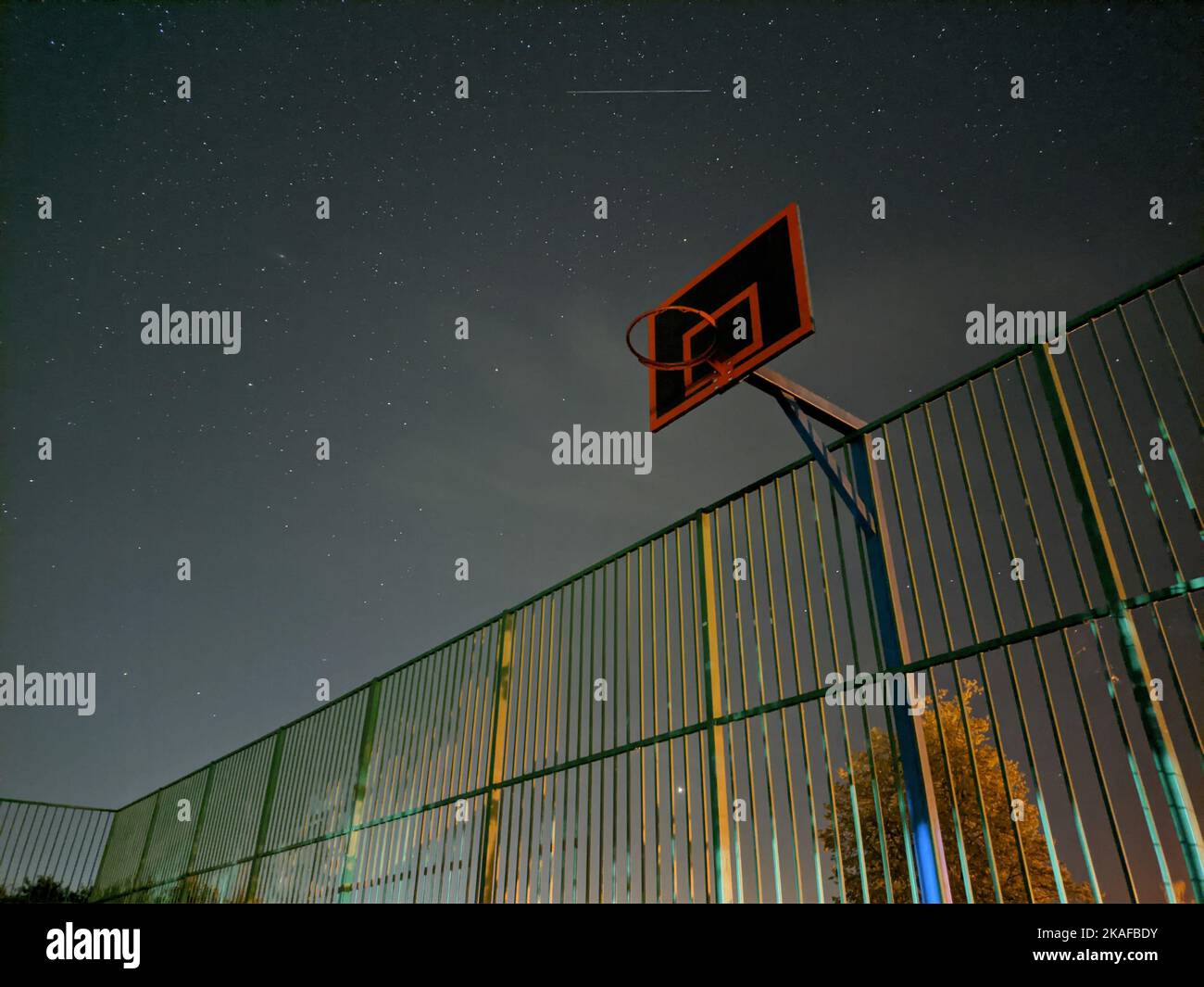 A low-angle of a basketball net outdoors with a starry night sky in the ...