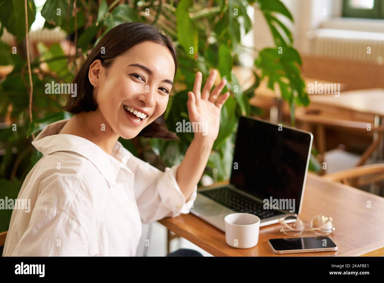 Portrait of beautiful young woman wave at you, say hello, greeting ...