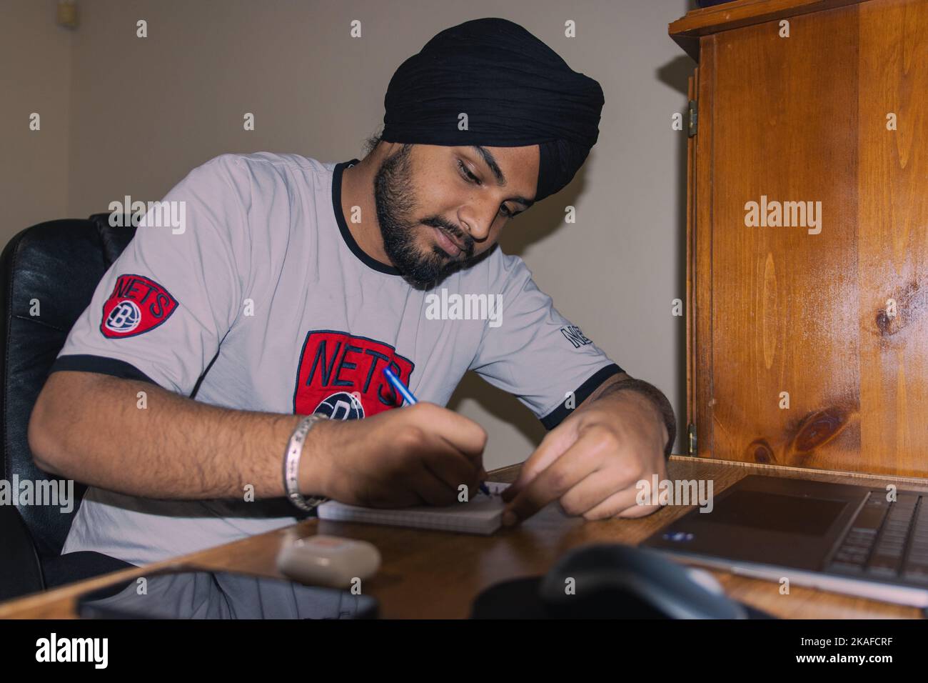 An Indian Sikh in a black pagari sitting at a desk holding a pen and ...