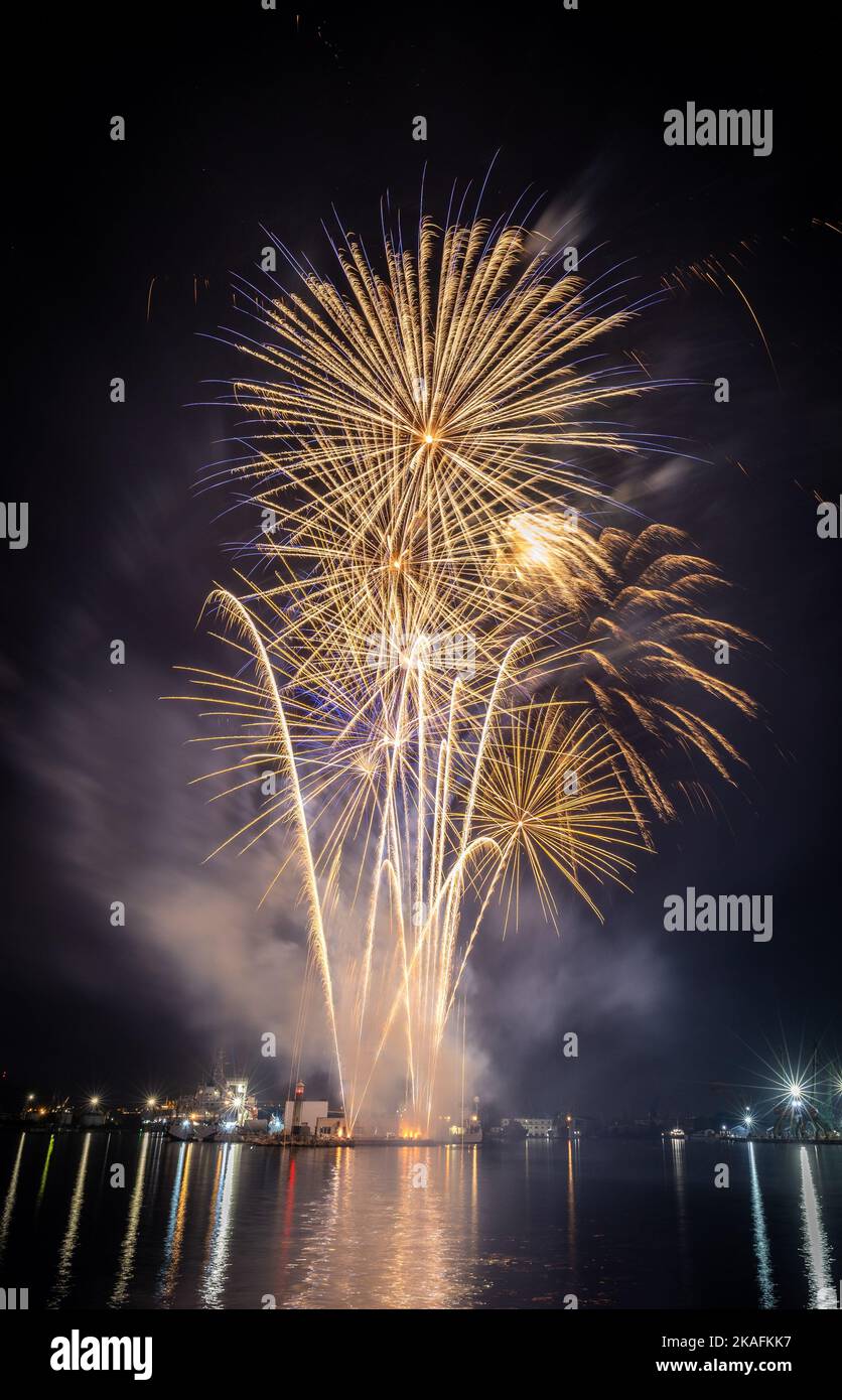 A vertical shot of golden fireworks reflecting on the surface of the ...