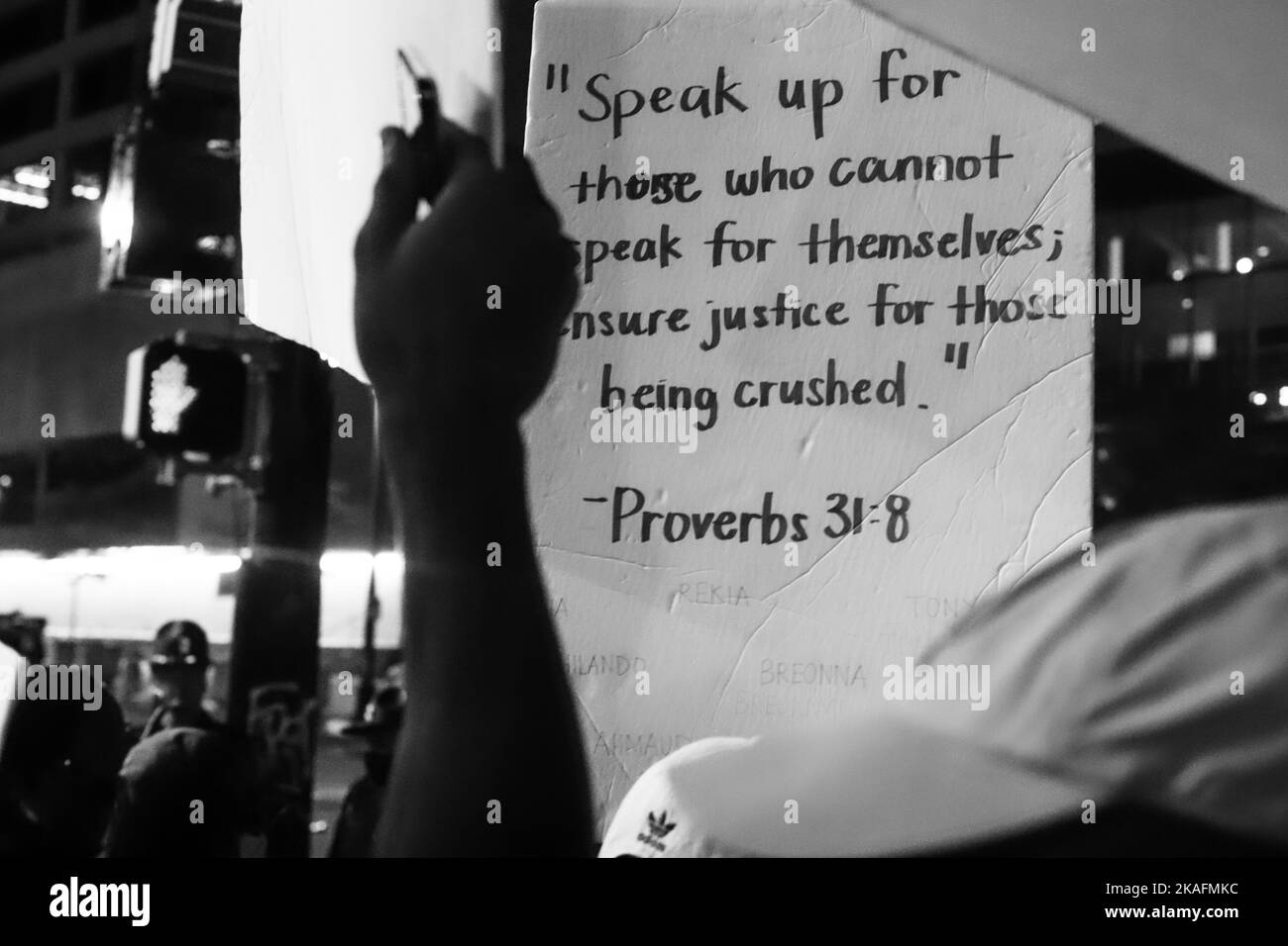 A grayscale of proverbs verse 31:8 handwritten on a sign raised high in ...