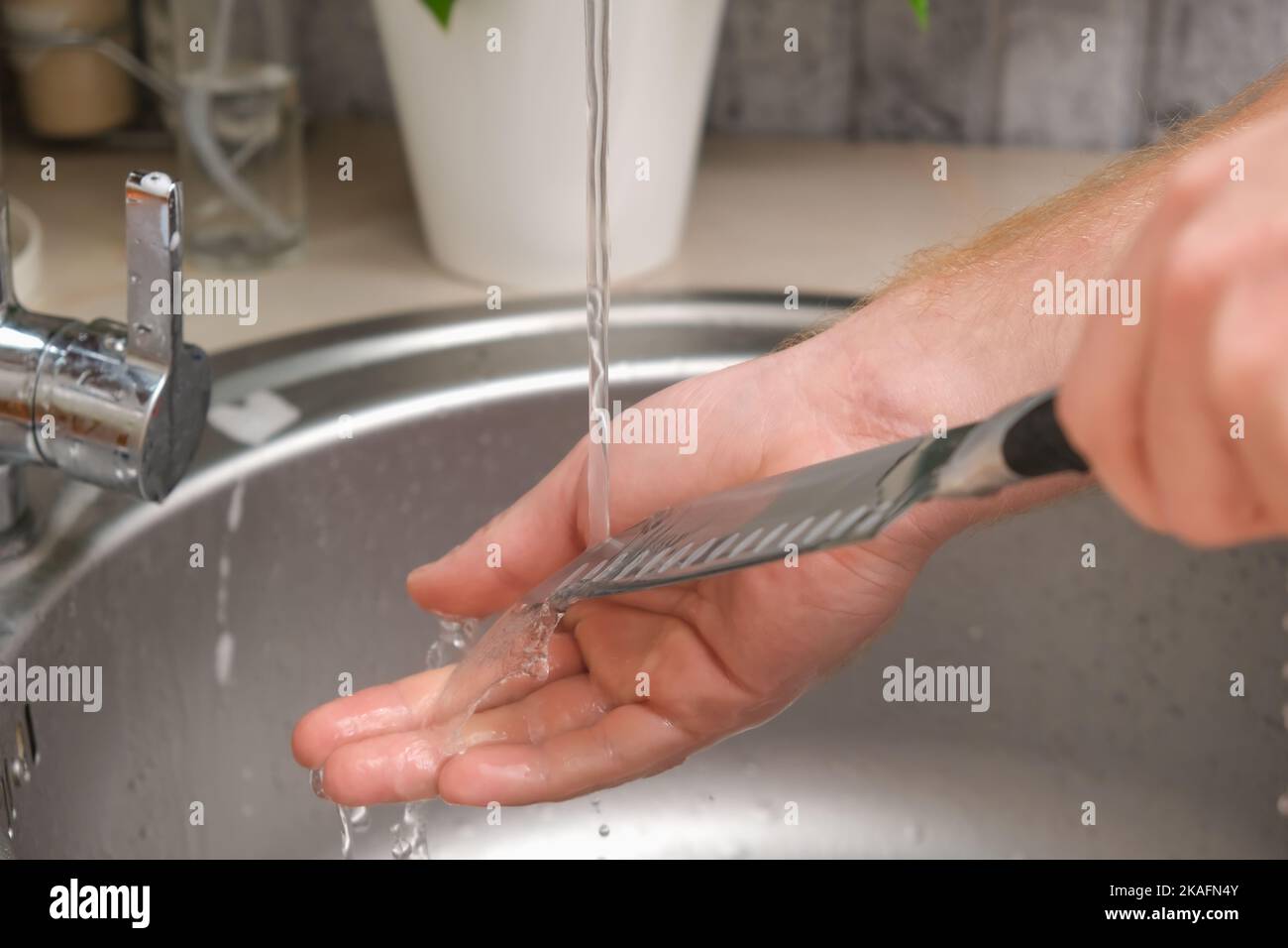 A man washes a sharp steel dirty kitchen knife with a sponge with ...